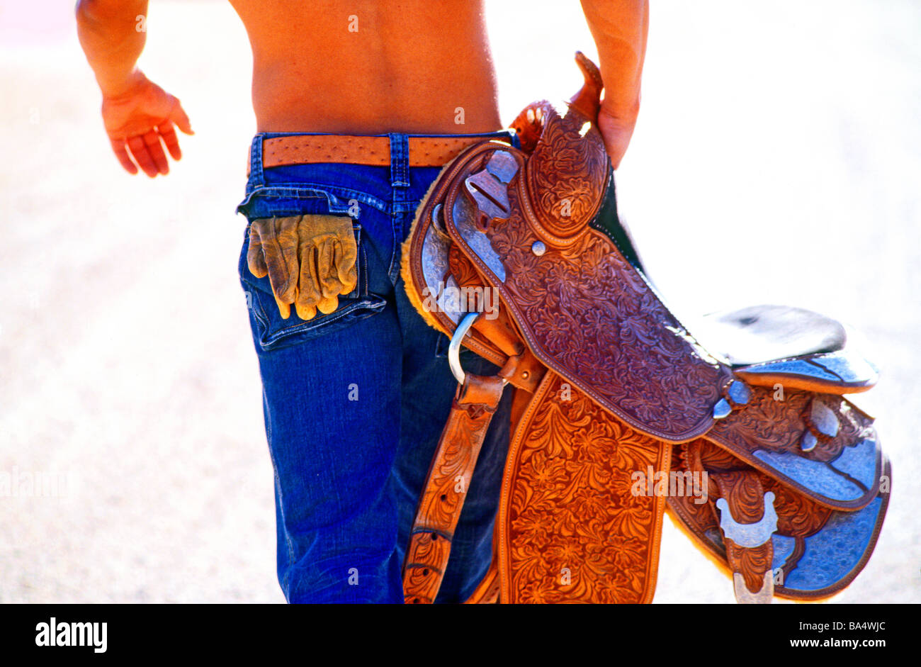 Young male ranch hand carries a custom leather saddle in the Arizona ...
