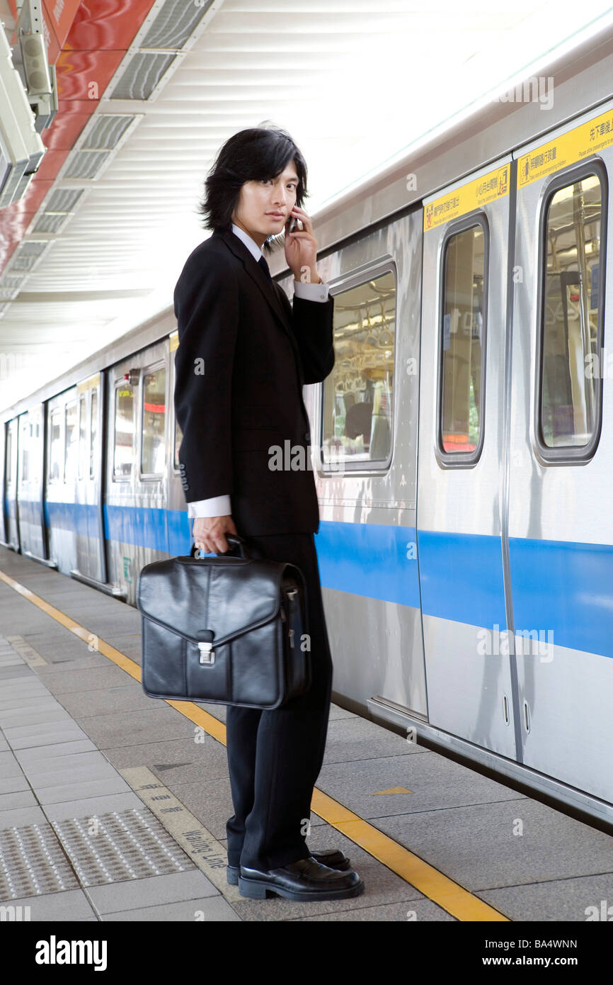 Businessman standing on train platform with briefcase using cell phone ...