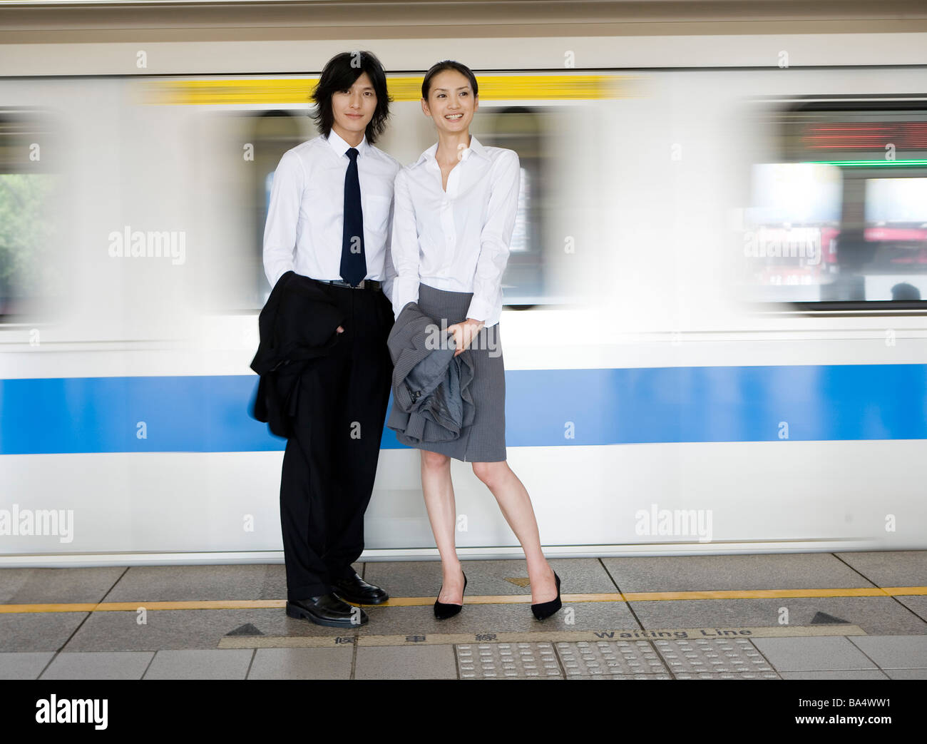 Businessman and businesswoman standing on train platform train passing ...
