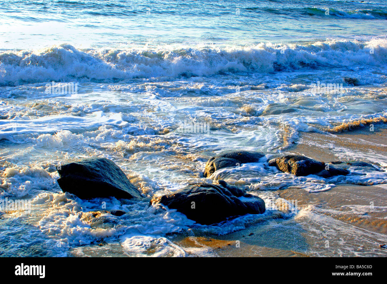 Waves on a tropical beach gently wash over rocks embedded in the sand ...