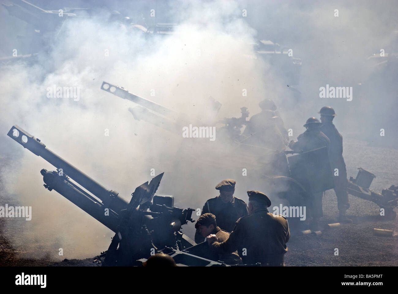 WW2 field guns being fired by crews with smoke blowing back across the ...