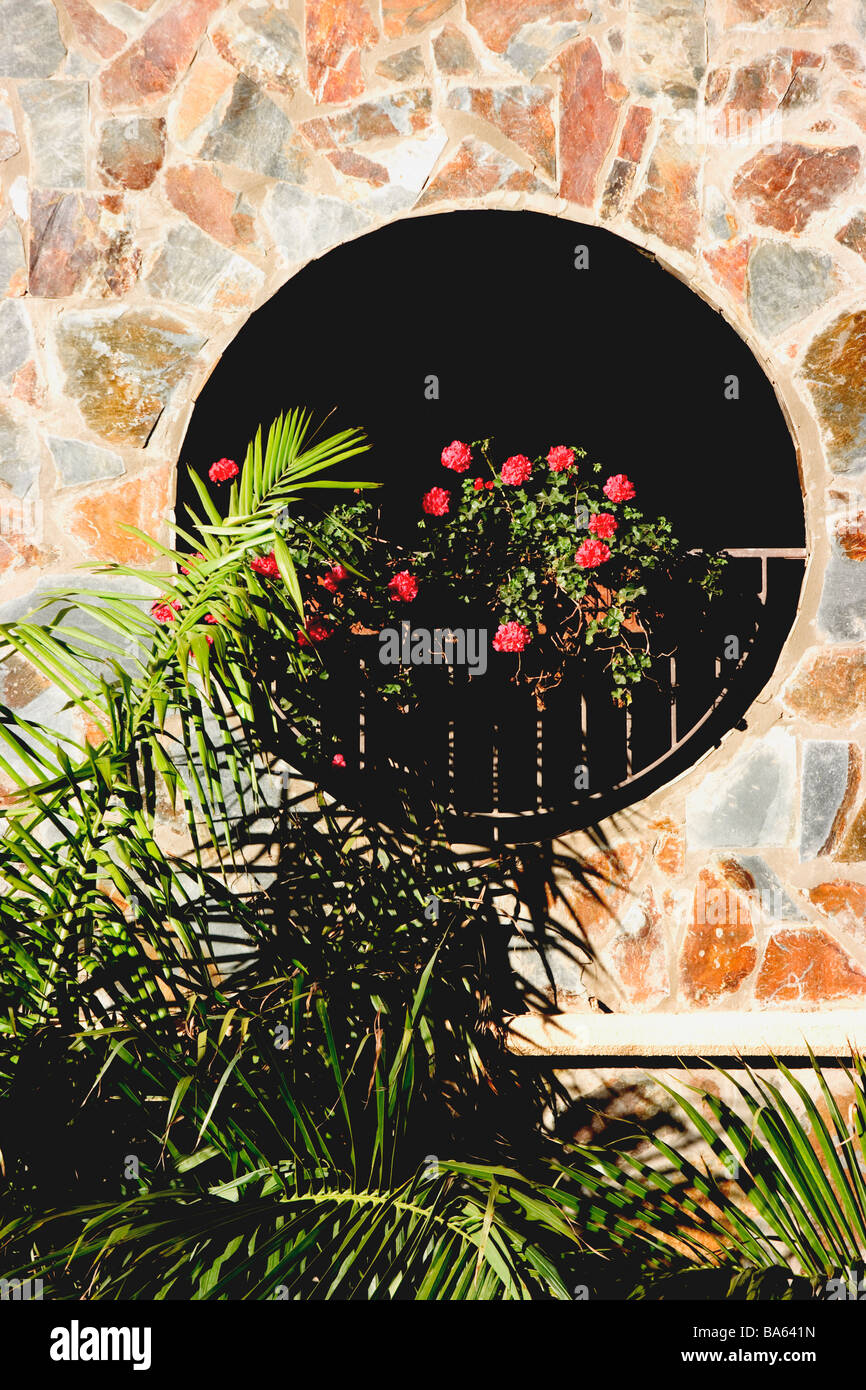 Red flowers on railings in circular opening in decorative stone wall in ...