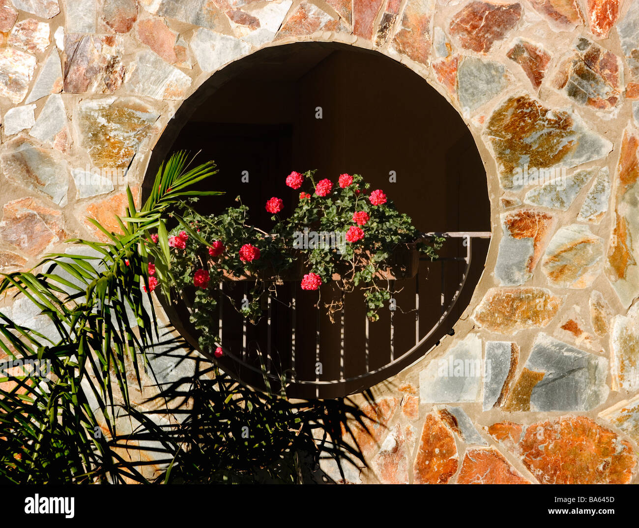 Red flowers on railings in circular opening in decorative stone wall in ...