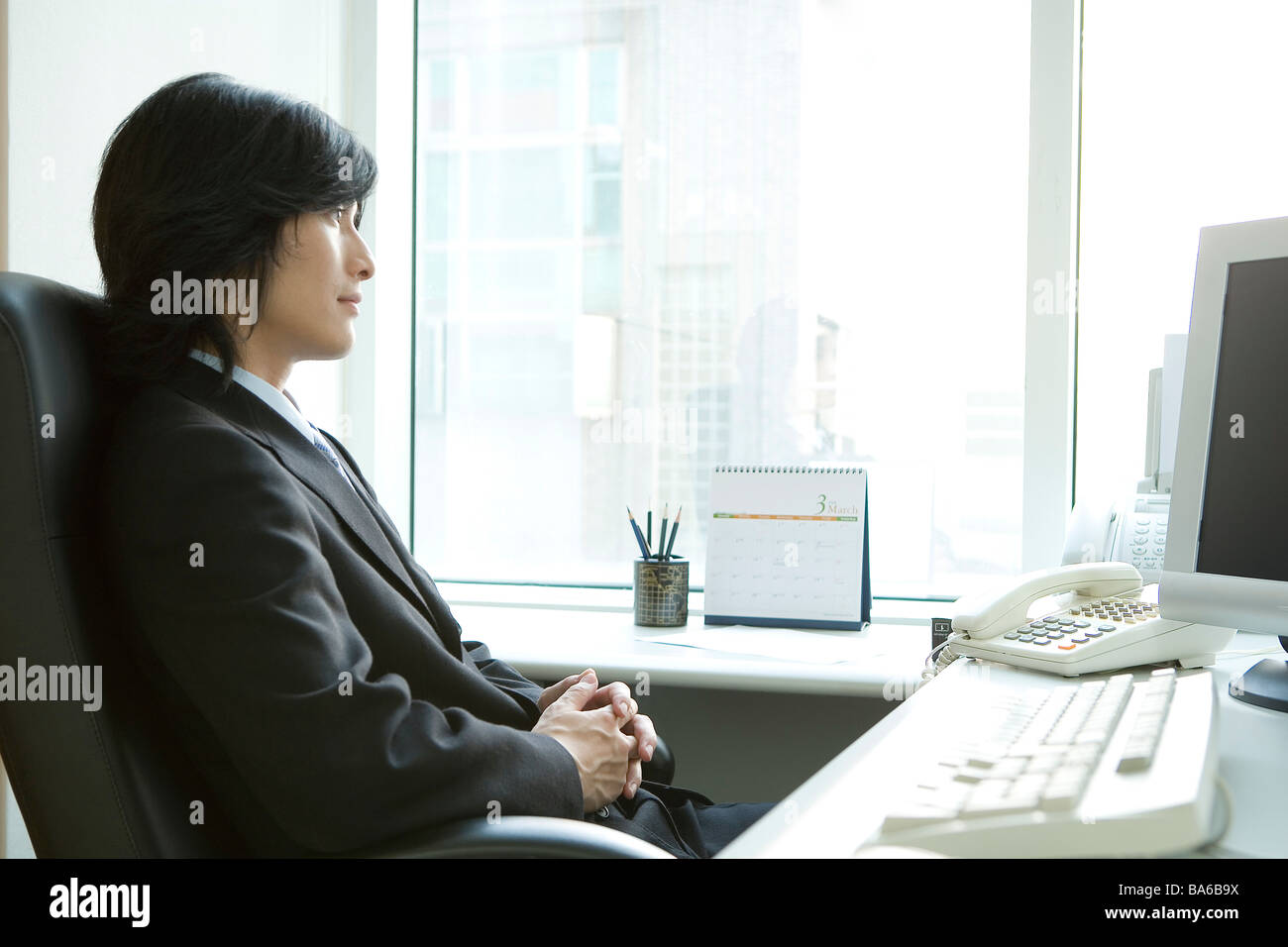 Side view of businessman sitting at desk looking out of window side ...