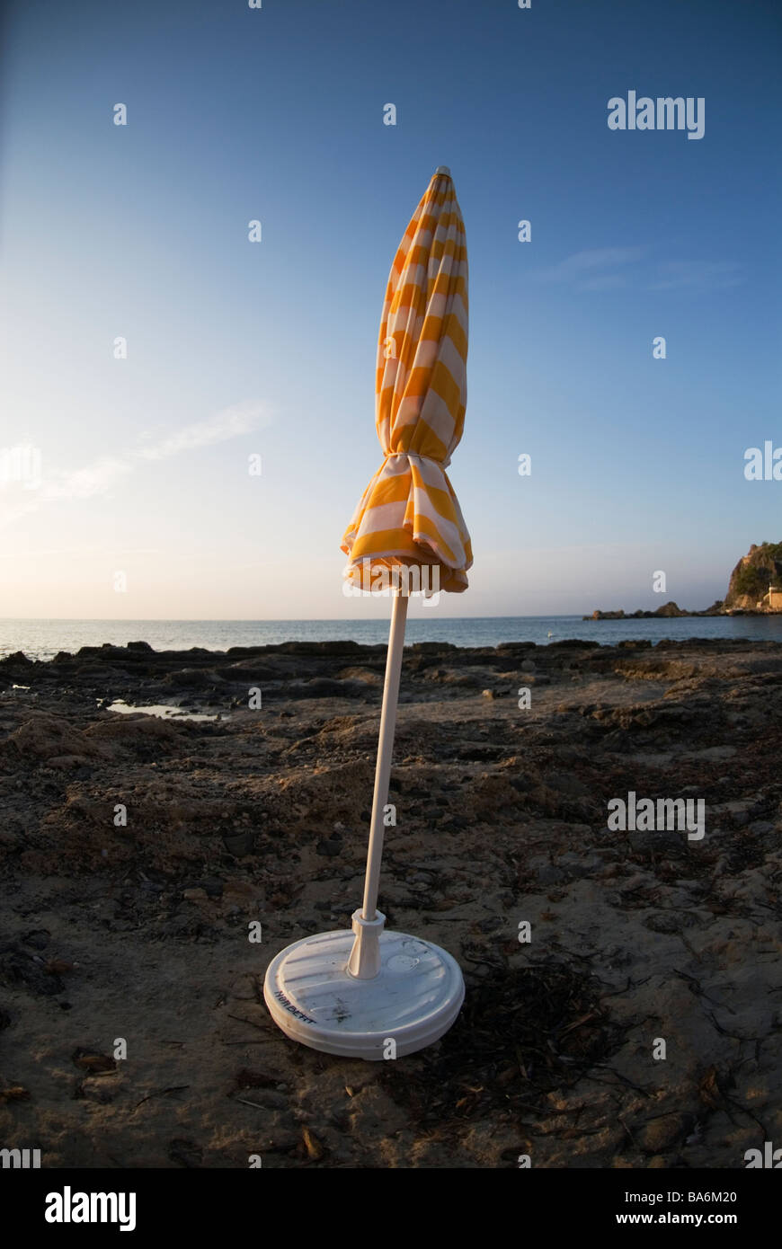 closed yellow and white striped parasol stands in small bay on the ...
