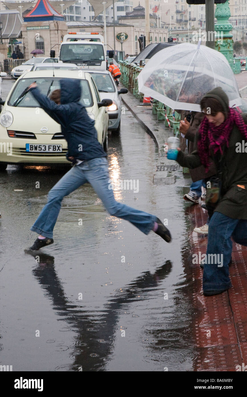 Woman jumping over puddle of rain water in road, Palace Pier, Brighton ...