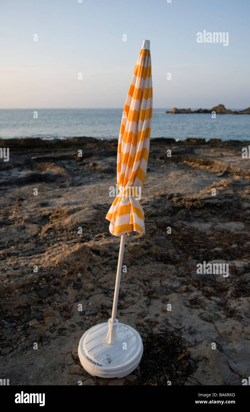 closed yellow and white striped parasol stands in small bay on the ...