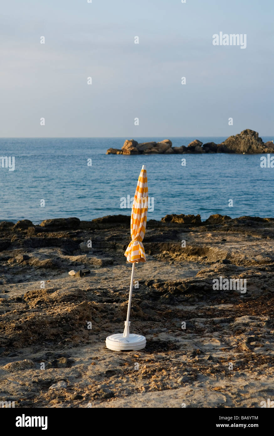 closed yellow and white striped parasol stands in small bay on the ...
