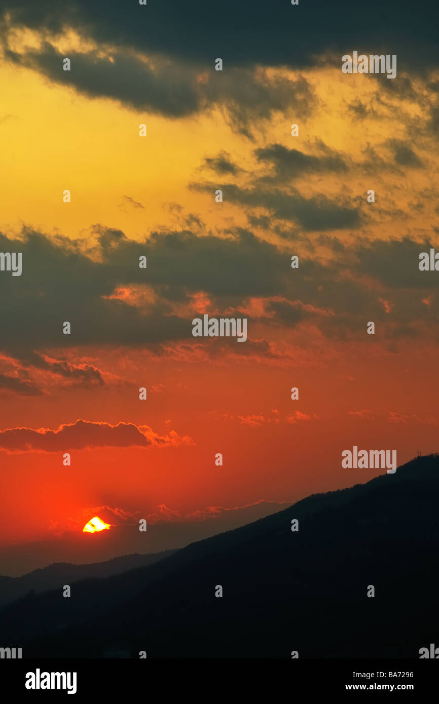 Distant setting sun disappearing over the horizon shrouded in clouds ...