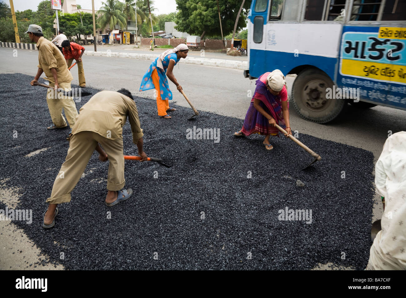 Male and female labourers / road workers spreading asphalt on a road in ...