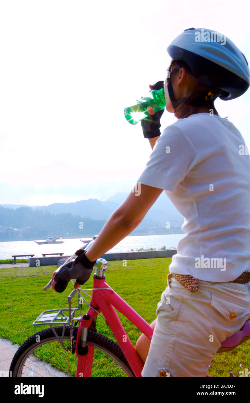Young woman drinking on bicycle with helmet rear view Stock Photo - Alamy