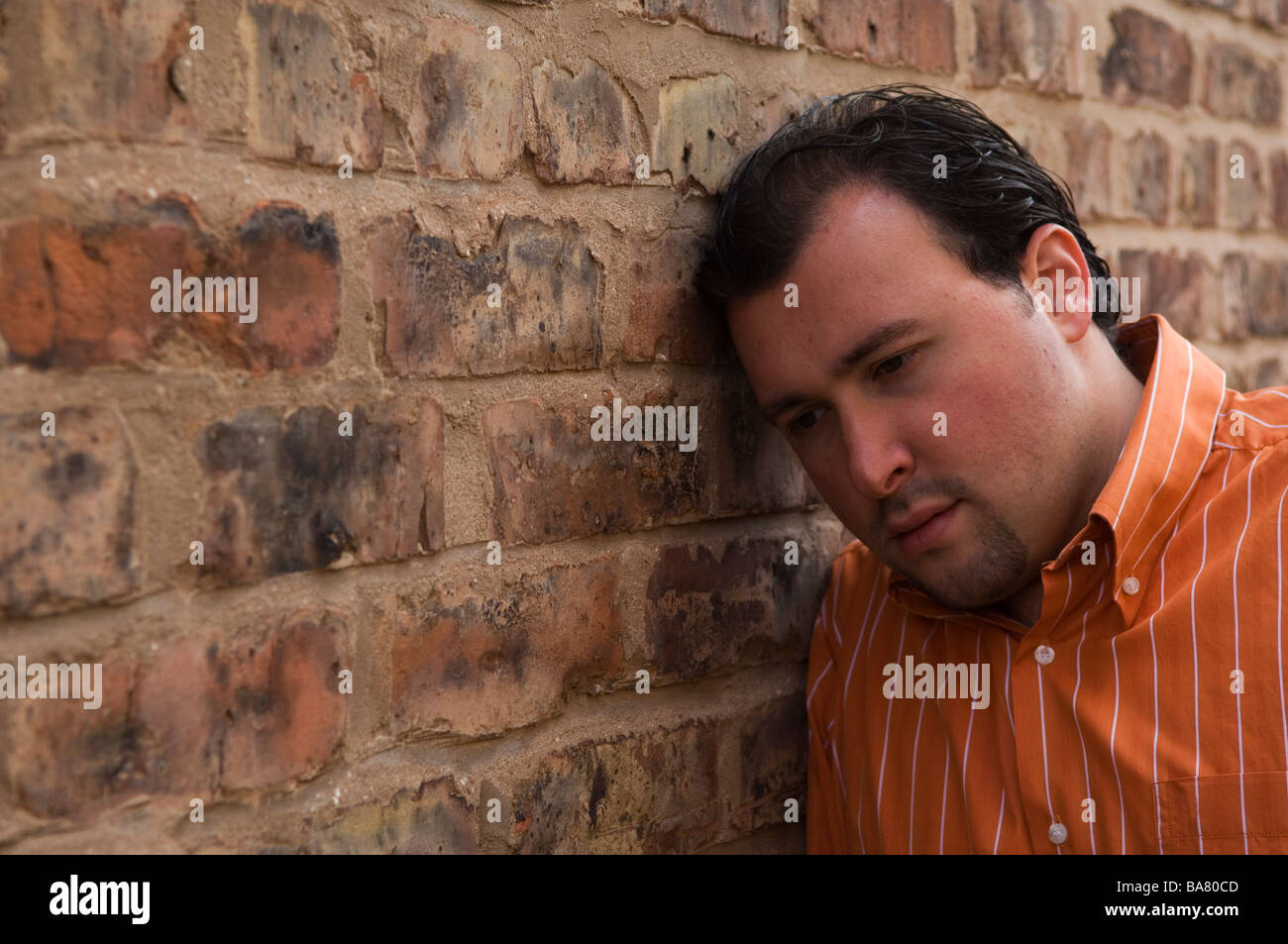Sad man leaning against a brick wall Stock Photo - Alamy