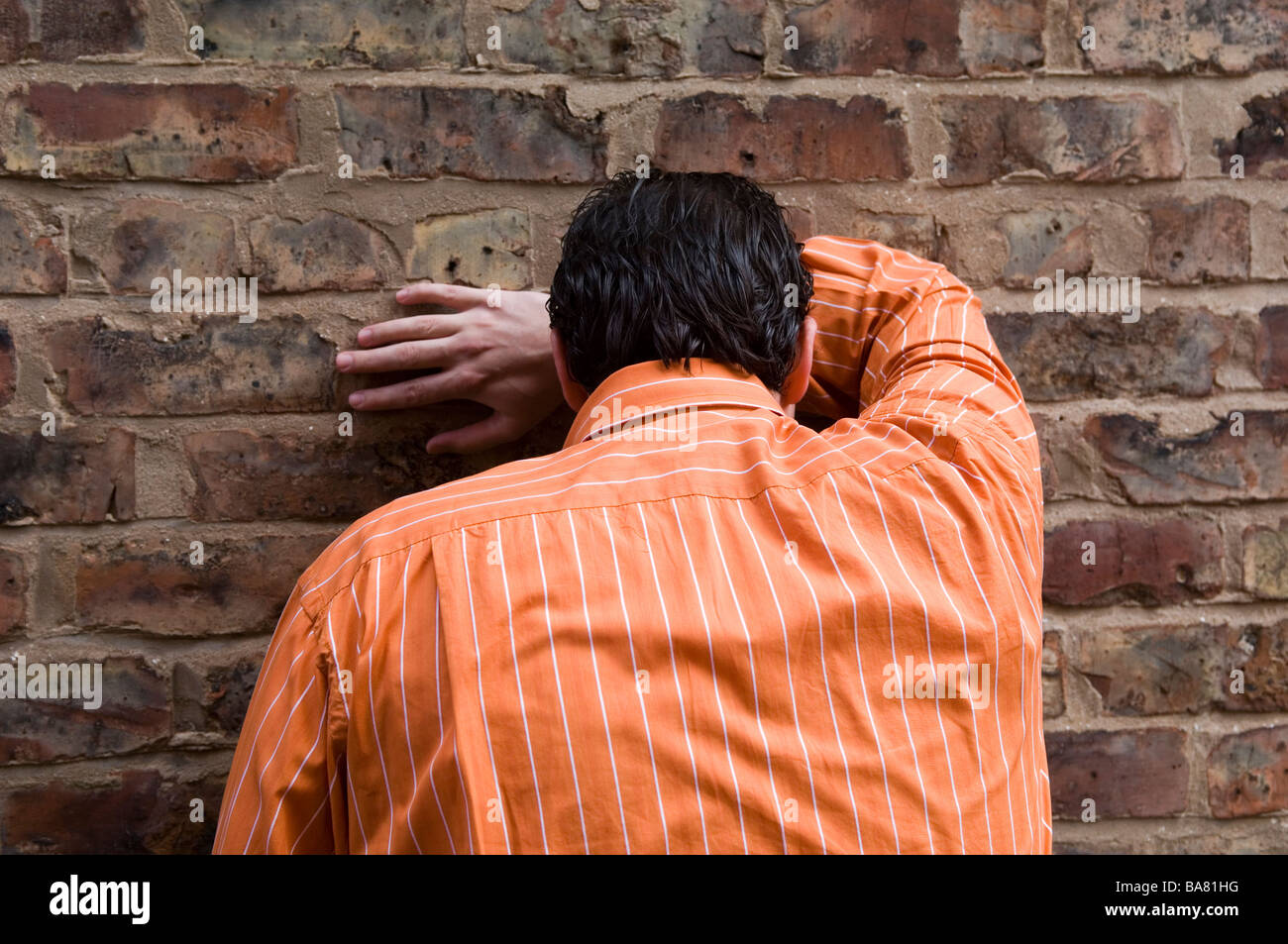 Man in orange stripy shirt hiding face against the rick wall Stock ...