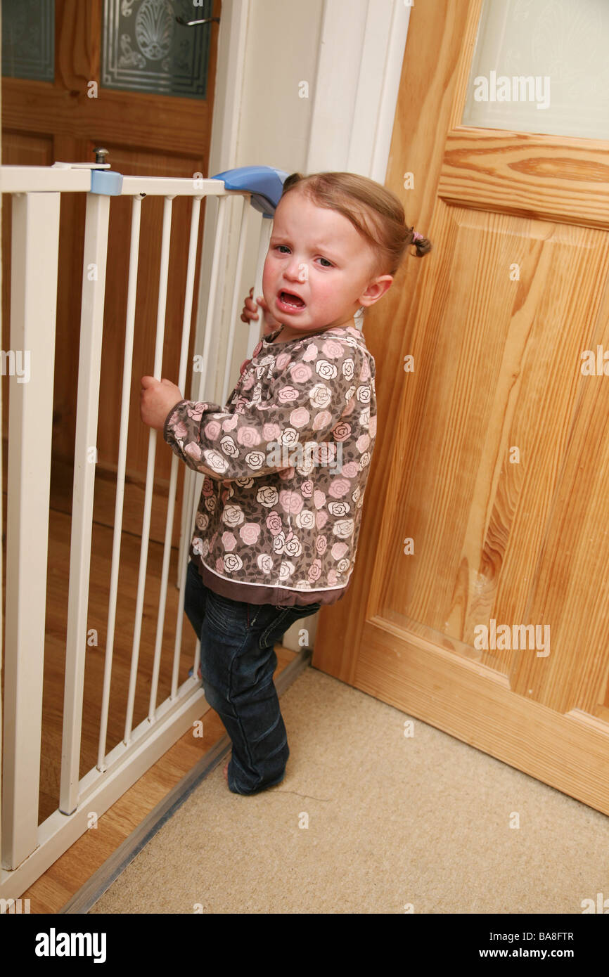 18 month girl holding onto the baby gate crying Stock Photo - Alamy