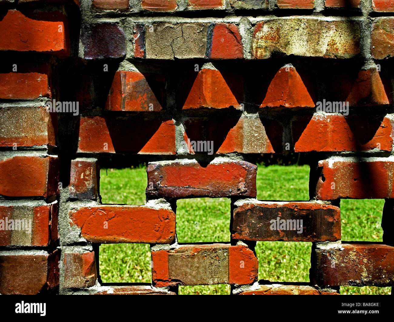 brick fence with spaced gaps in wall and bright green grass behind ...