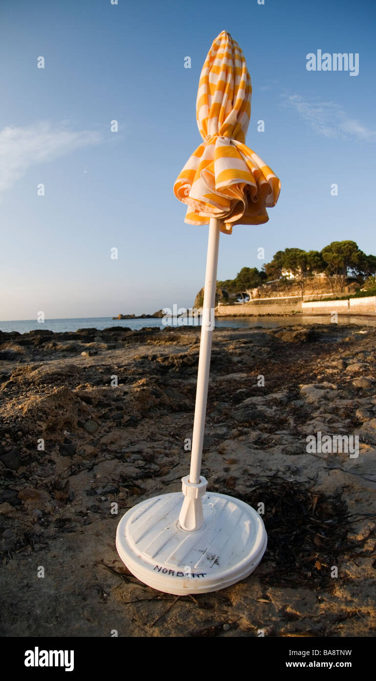 closed yellow and white striped parasol stands in small bay on the ...