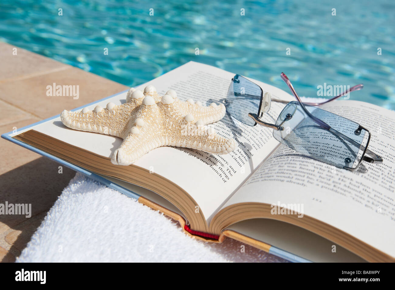 Book and sunglasses by swimming pool Stock Photo - Alamy