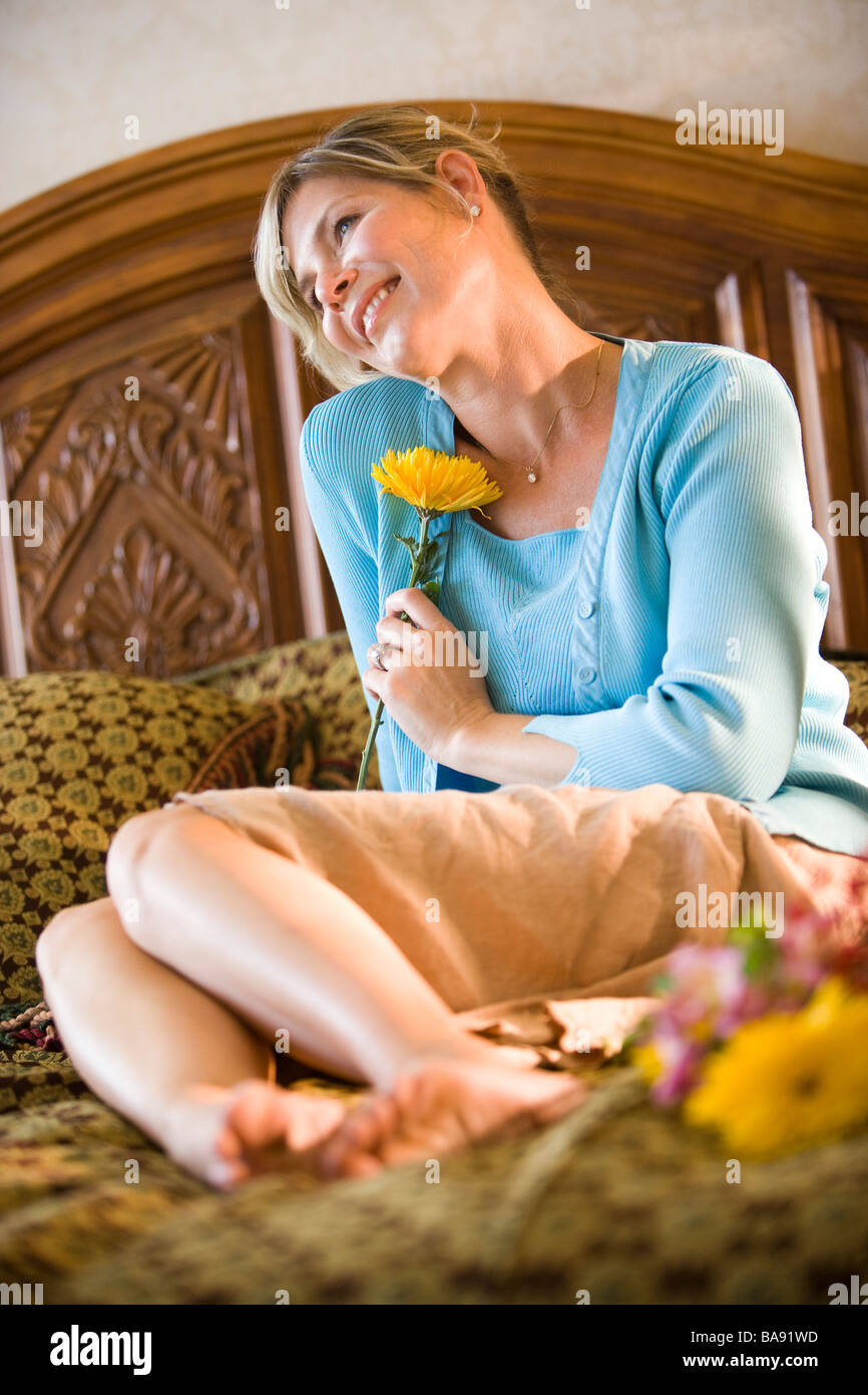 Mid-adult woman holding flower on bed, smiling Stock Photo - Alamy