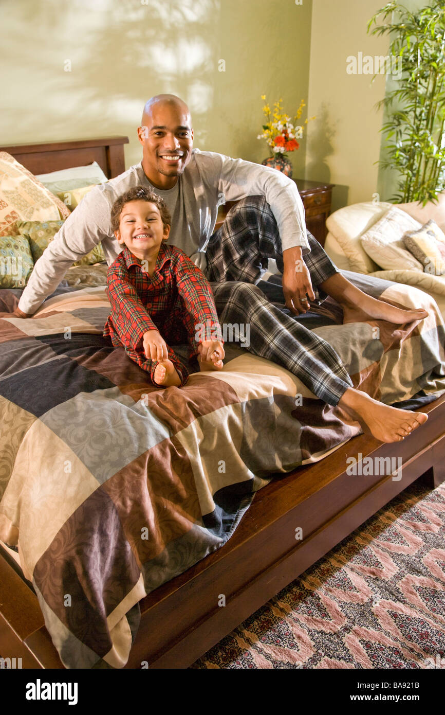 African-American father and son sitting on bed in pajamas Stock Photo ...