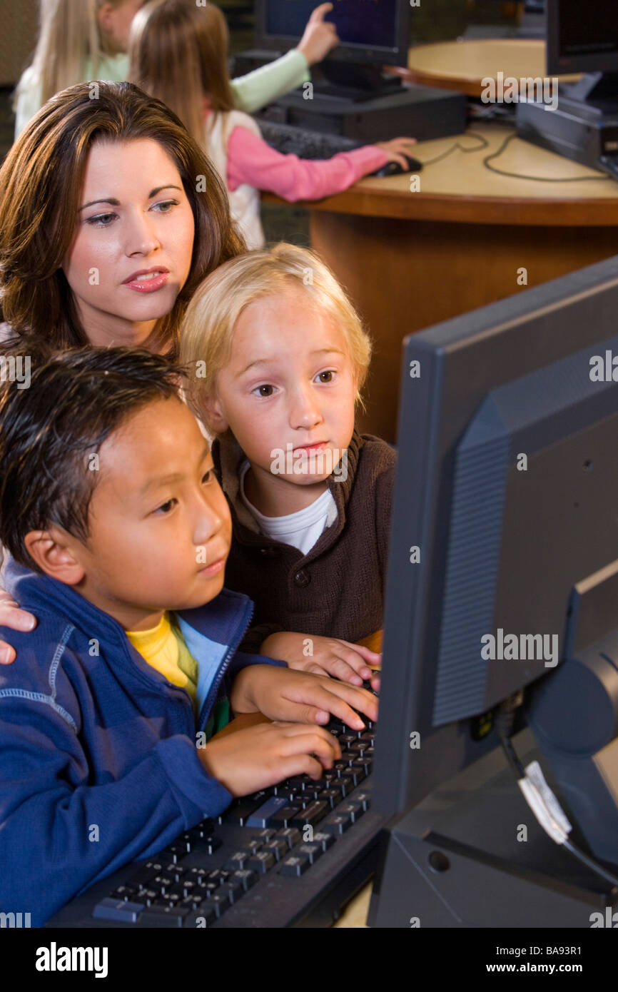 Elementary school teacher and kids looking at computer in library Stock ...