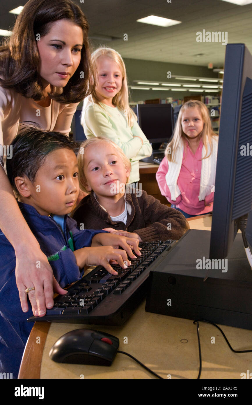 Elementary school teacher and kids looking at computer in library Stock ...