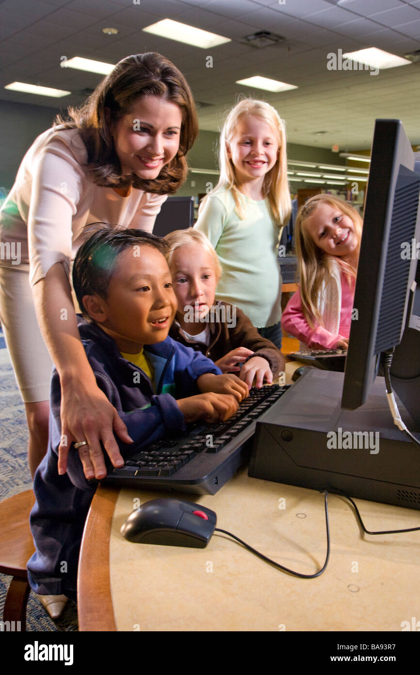 Elementary school kids and teacher looking at computer in library Stock ...