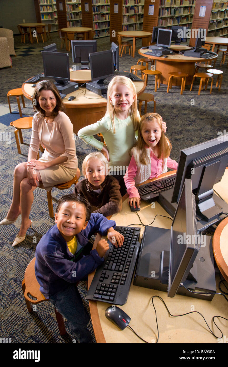 Portrait of teacher and elementary school kids at computer in library ...
