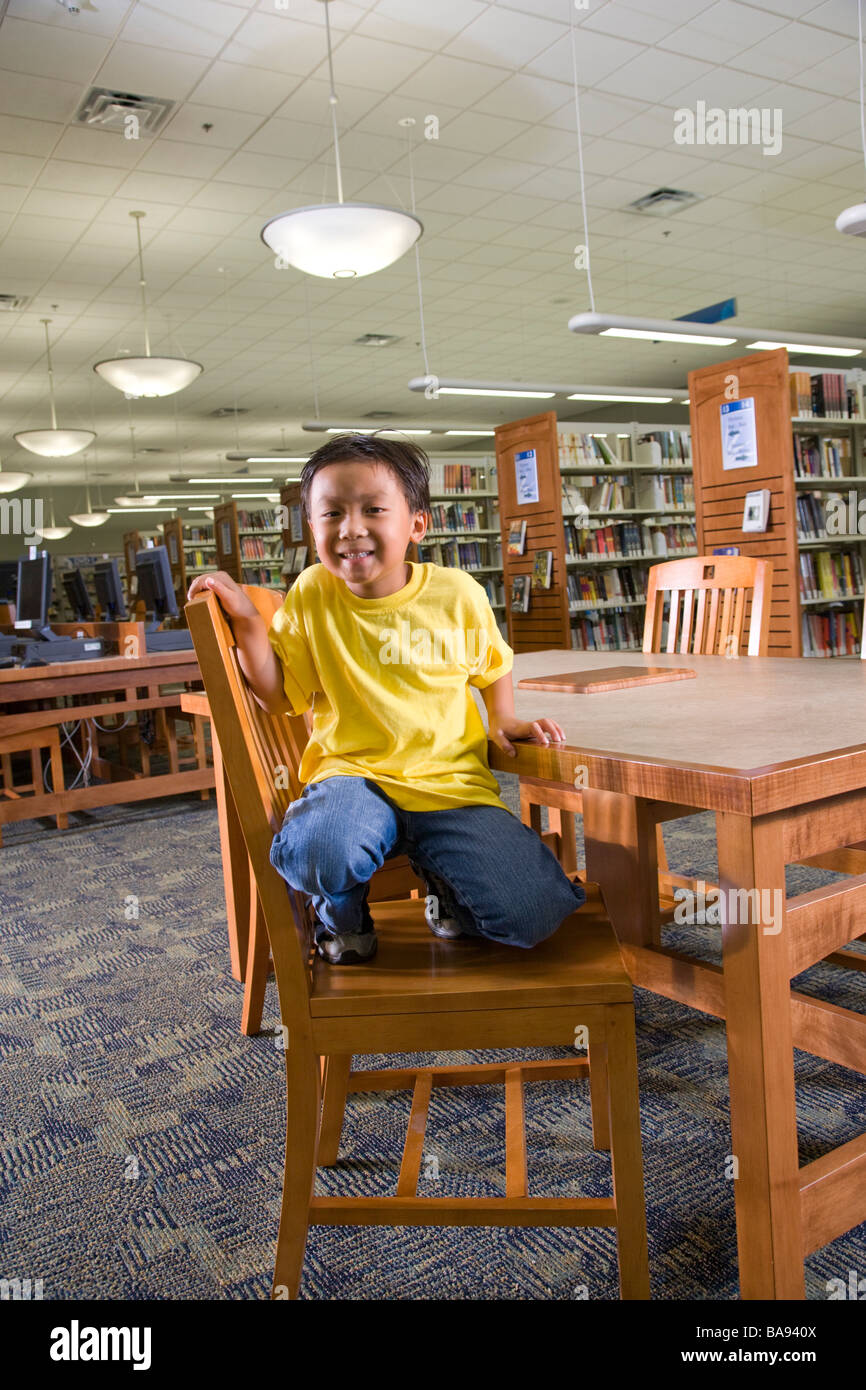 Asian boy crouching on chair in school library Stock Photo - Alamy