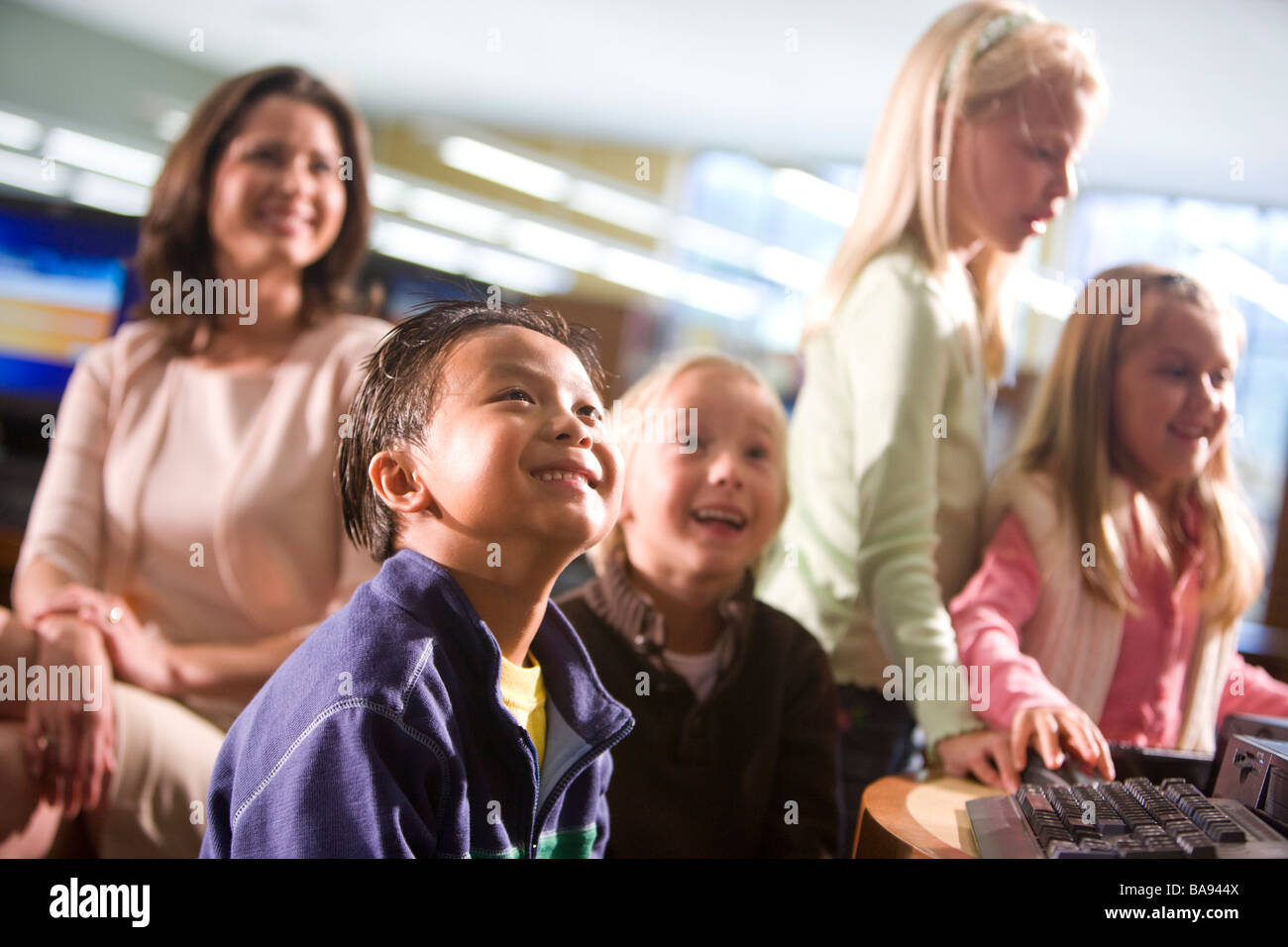 Elementary school teacher in library with kids looking at computer ...