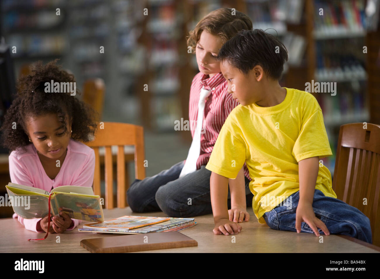 Three elementary school children sitting at table in library Stock ...