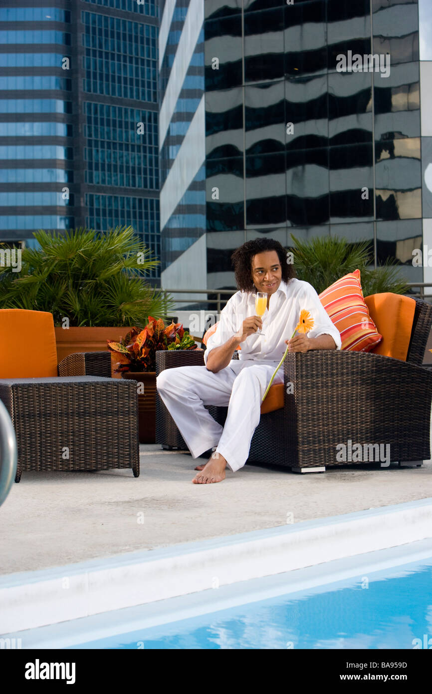 African-American man sitting on rooftop terrace by swimming pool in ...