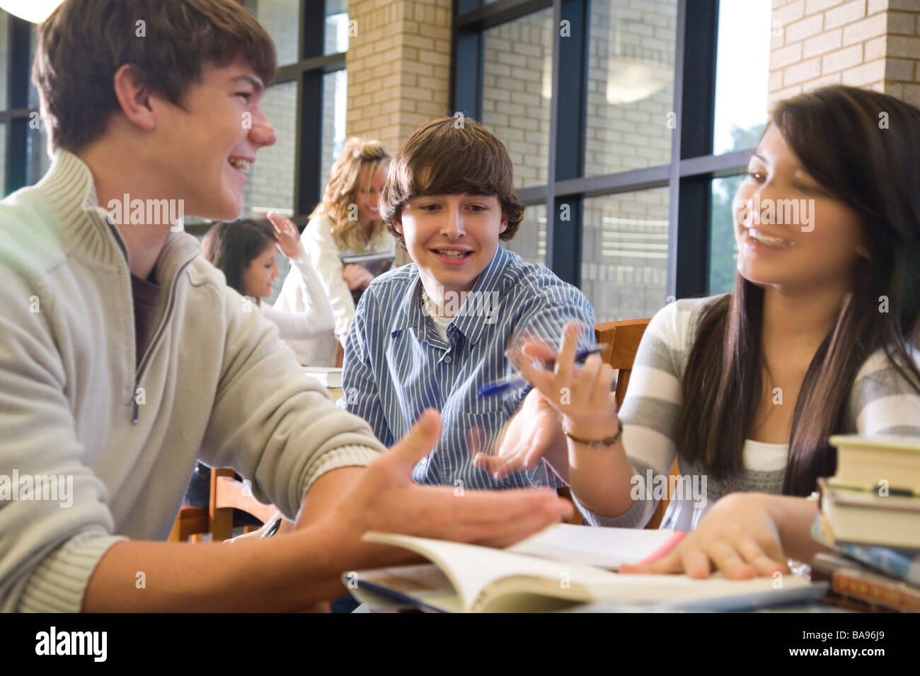 Three teenage students discussing in library Stock Photo - Alamy