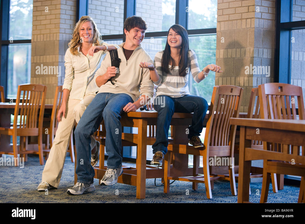 Three teenage students sitting on table in library Stock Photo - Alamy