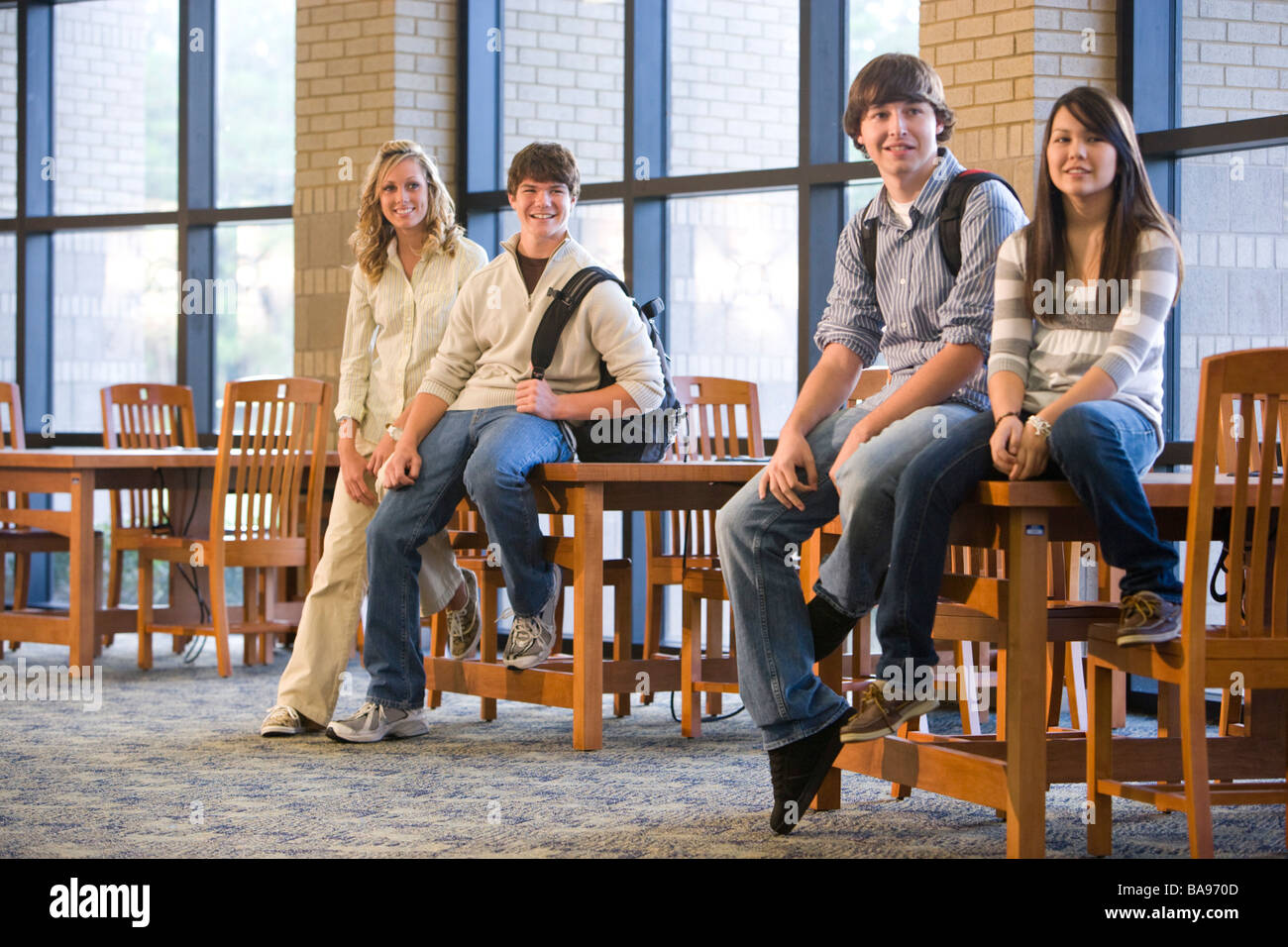 Four teenage students sitting on table in library Stock Photo - Alamy