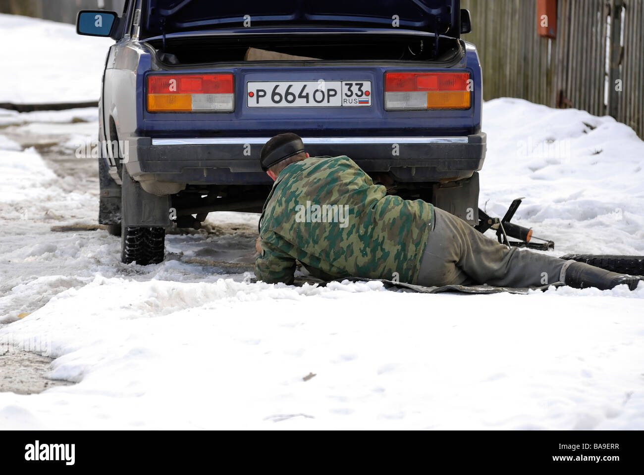The man repairs the car laying on snow Stock Photo - Alamy