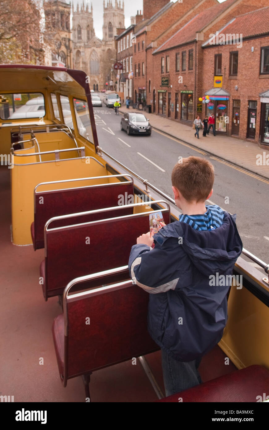 A young boy on the open top deck of a sightseeing bus travelling ...
