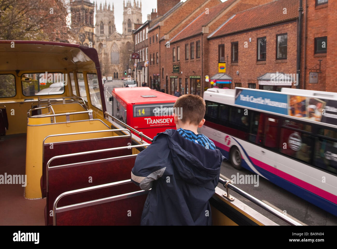 A young boy on the open top deck of a sightseeing bus travelling ...