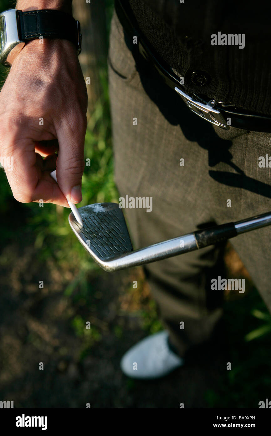 A Scandinavian man cleaning the blade of his golf club with a peg ...