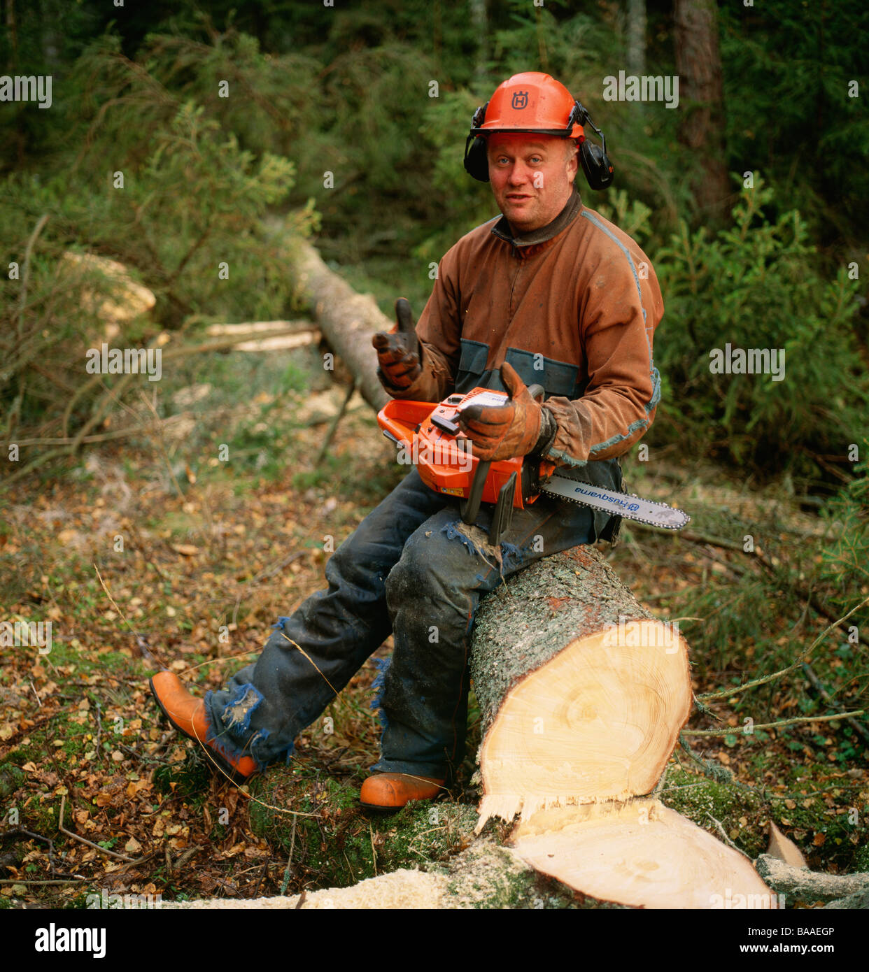 Mid adult man sitting on chopped tree trunk with chainsaw portrait ...