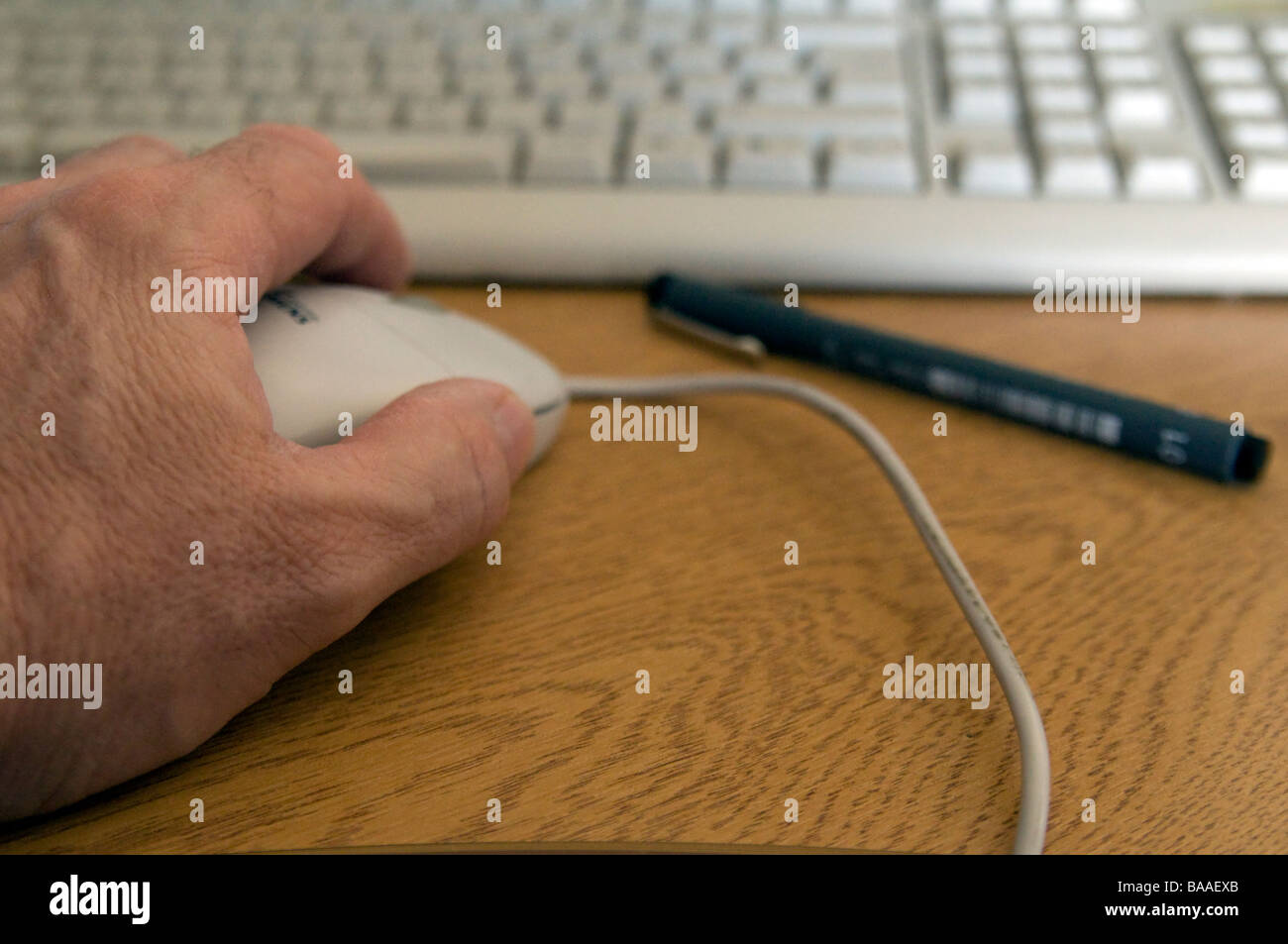 Mans hand on computer mouse at a desk with keyboard in the distance ...
