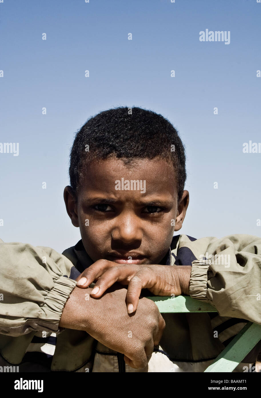 Young Moroccan boy hanging on a fence reflecting and looking straight ...