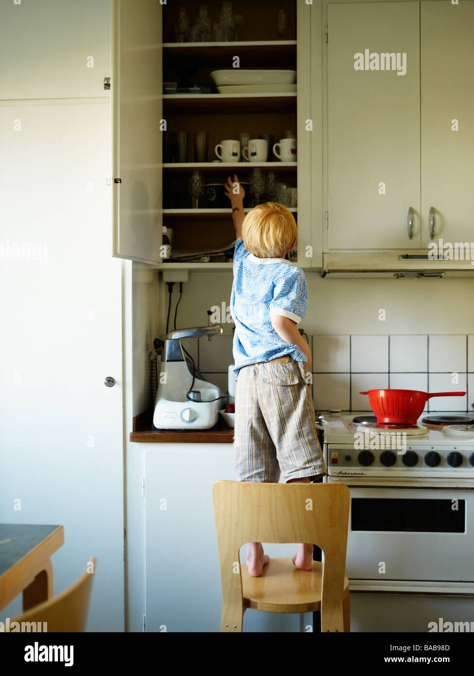 Boy standing on a chair reaching for a glass Sweden Stock Photo - Alamy