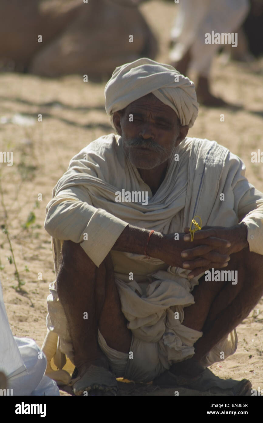 Indian man in traditional dress, squatting on the ground at Pushkar ...