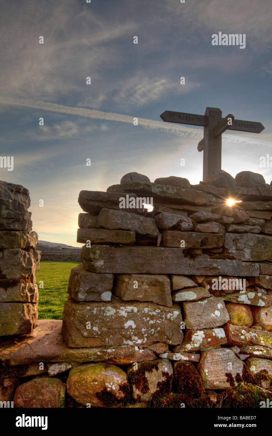 A dry stone wall with a stile just big enough to get through and a sign ...