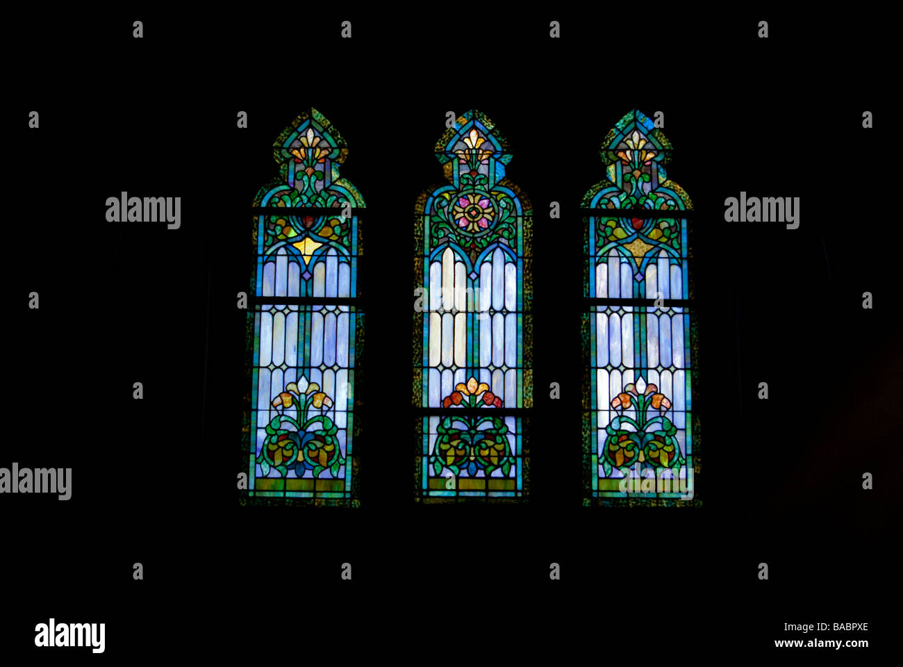 Three restored stained glass windows lit from the outside in a church ...