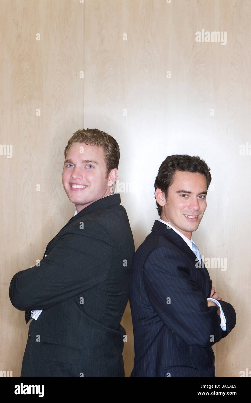 Two Happy business men standing back to back with their arms folded in ...