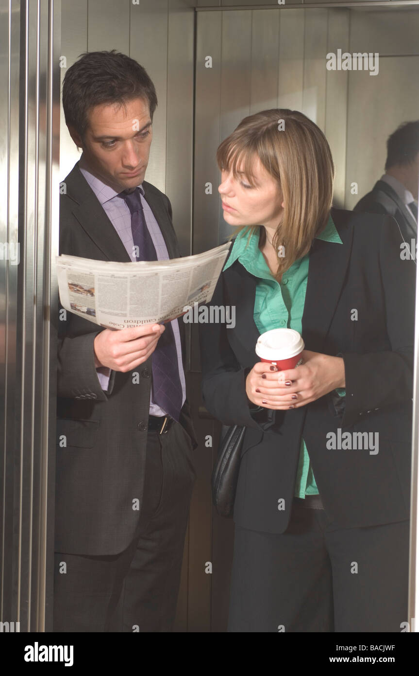 Businessman and a businesswoman reading a newspaper in an elevator ...
