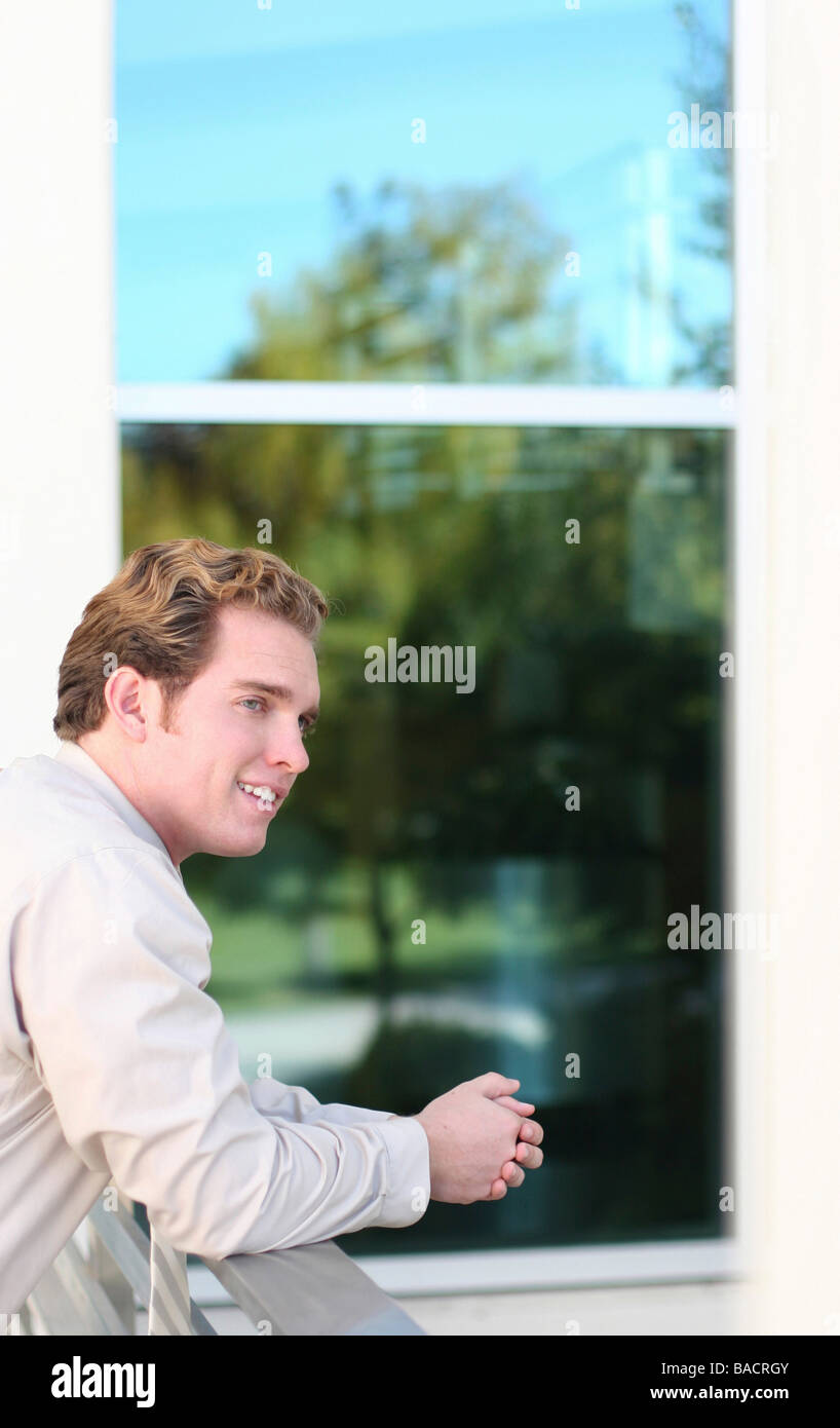 Business man smiles as he leans over glass wall in front of building ...