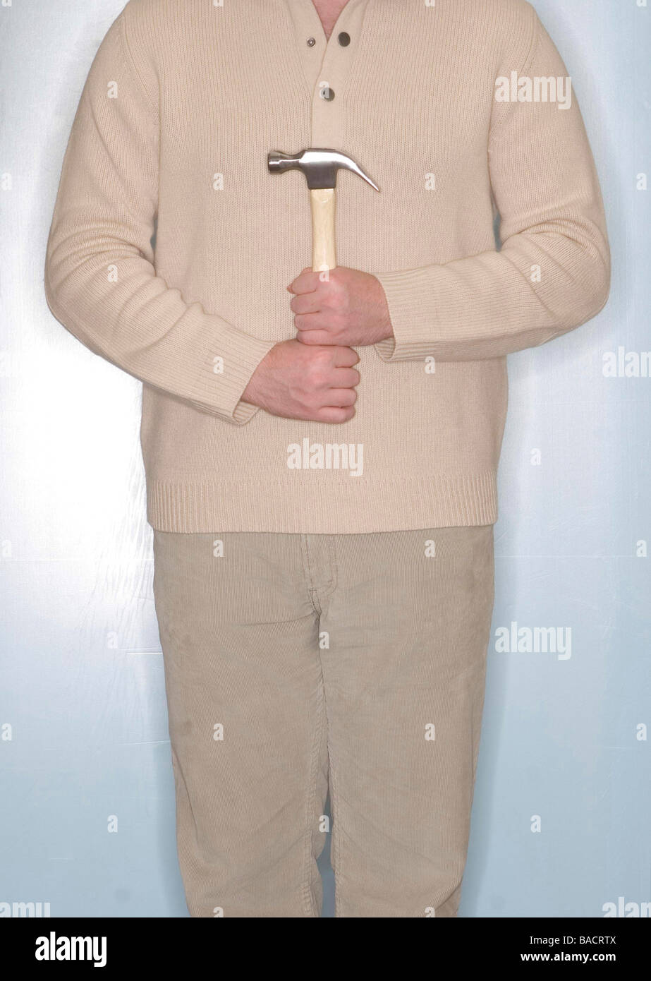 Man dressed in off-white clothing holds a hammer in front of his body ...