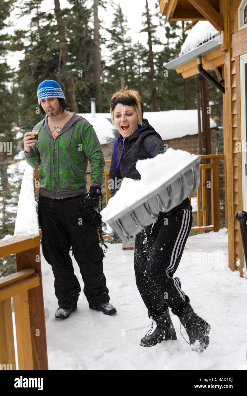 Young Woman scooping snow with shovel while young man watches in ...